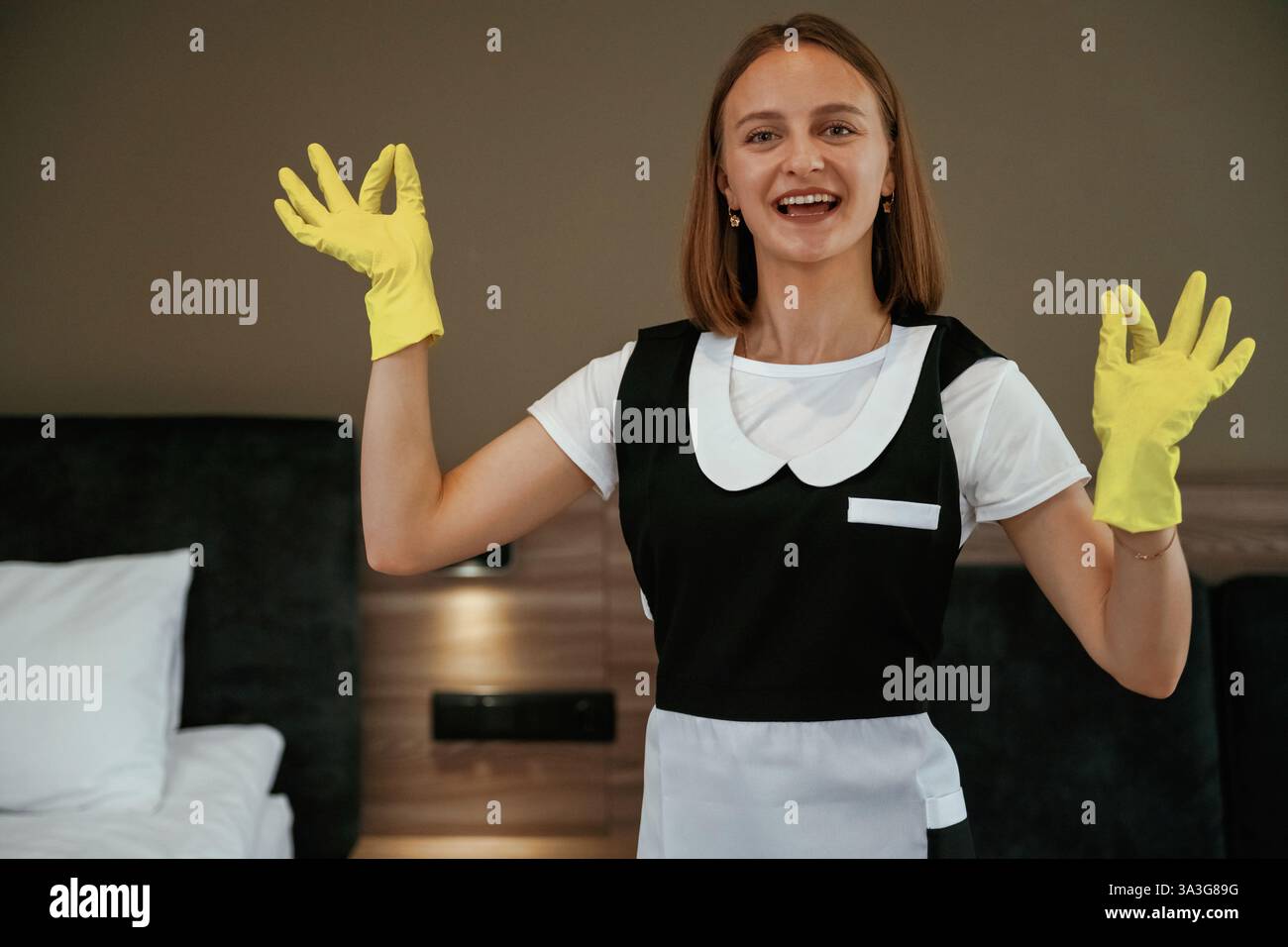 Cleaning is finished, in yellow gloves. Young chambermaid is in hotel ...