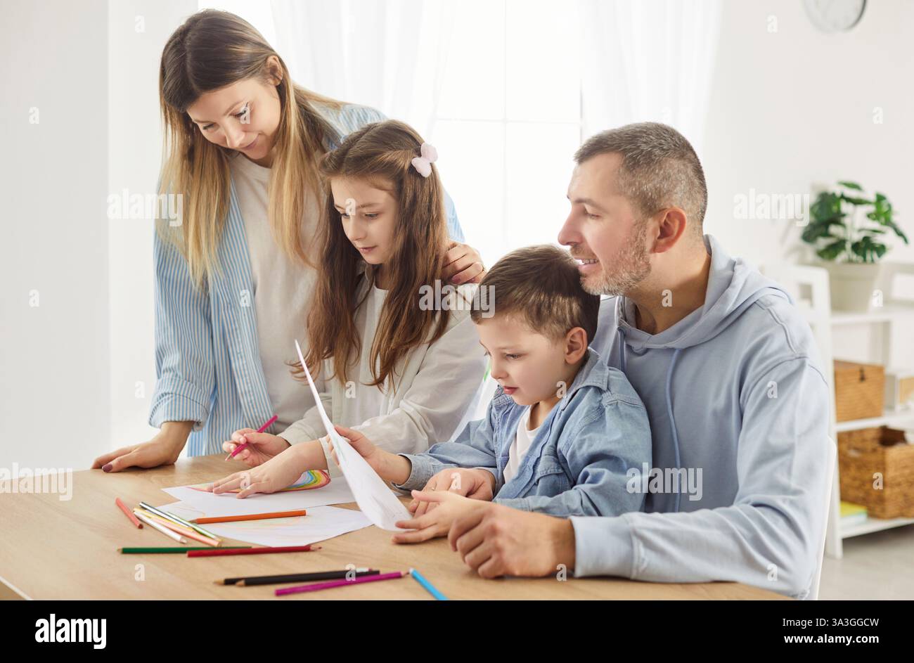 Caring parents and two children sitting at desk, drawing and coloring ...