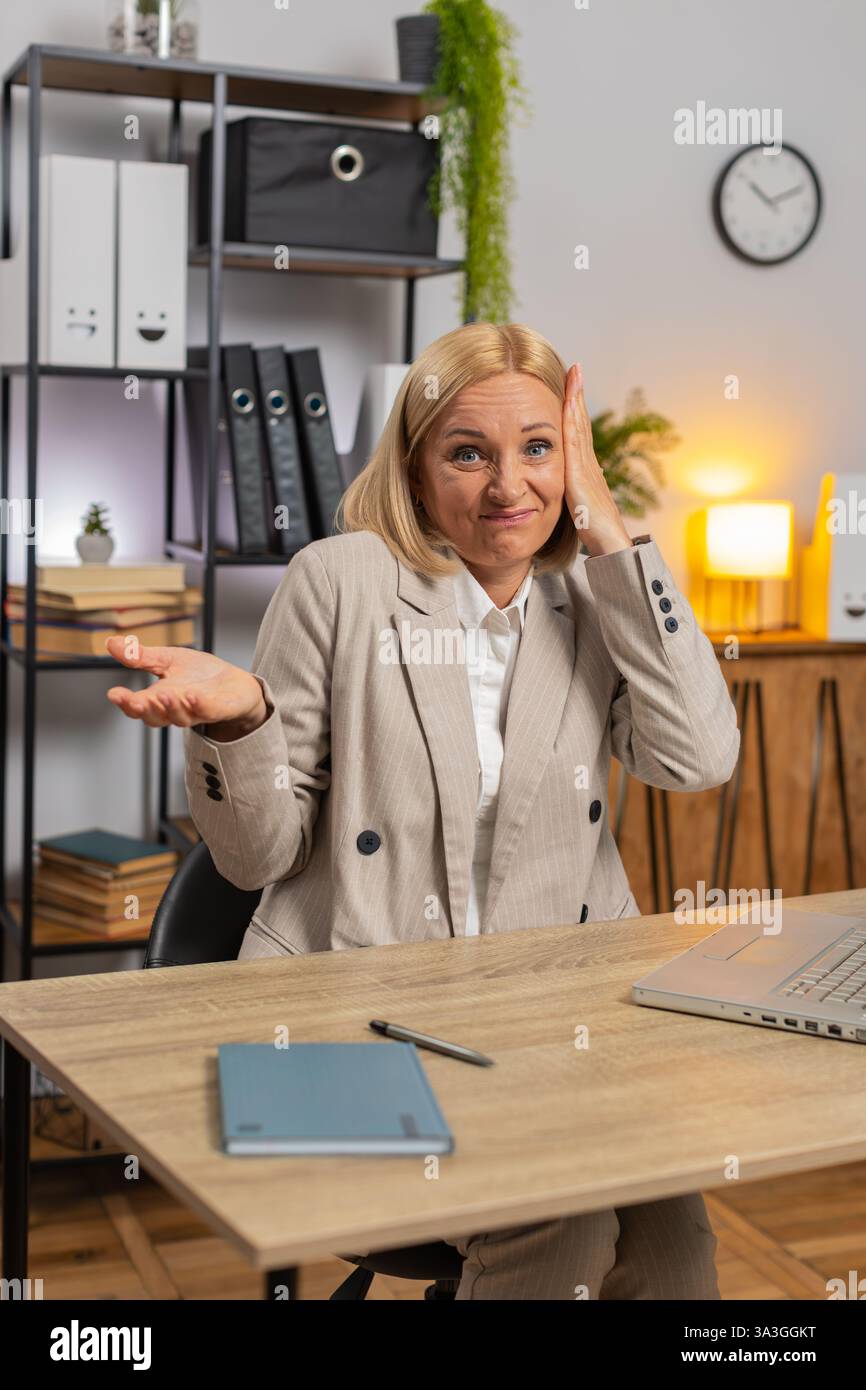 I don't know what to say. Confused mature businesswoman in suit working on laptop at home office ...