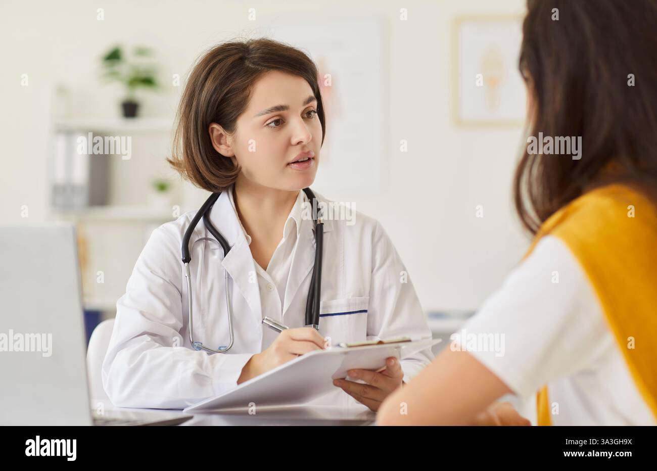 Positive young female practitioner doctor in clinic talking to patient ...