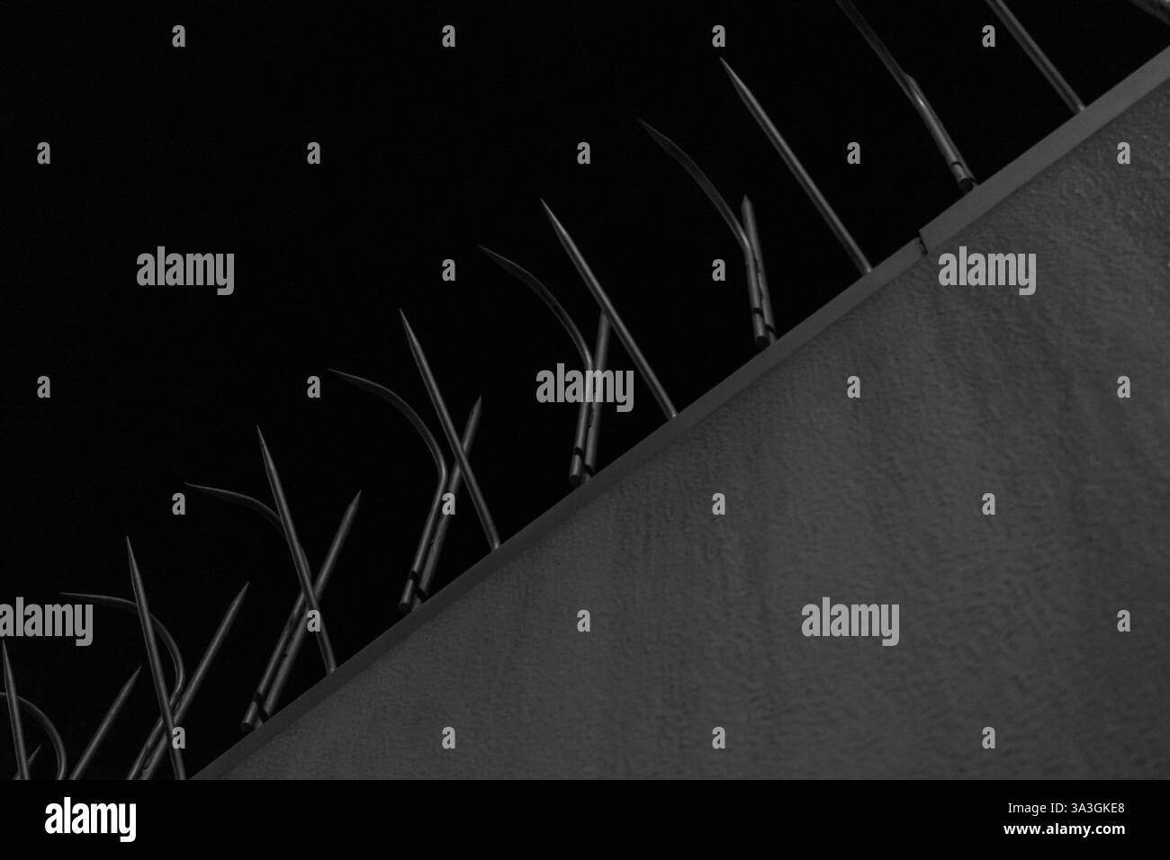 A black-and-white image of a concrete wall with sharp metal security ...