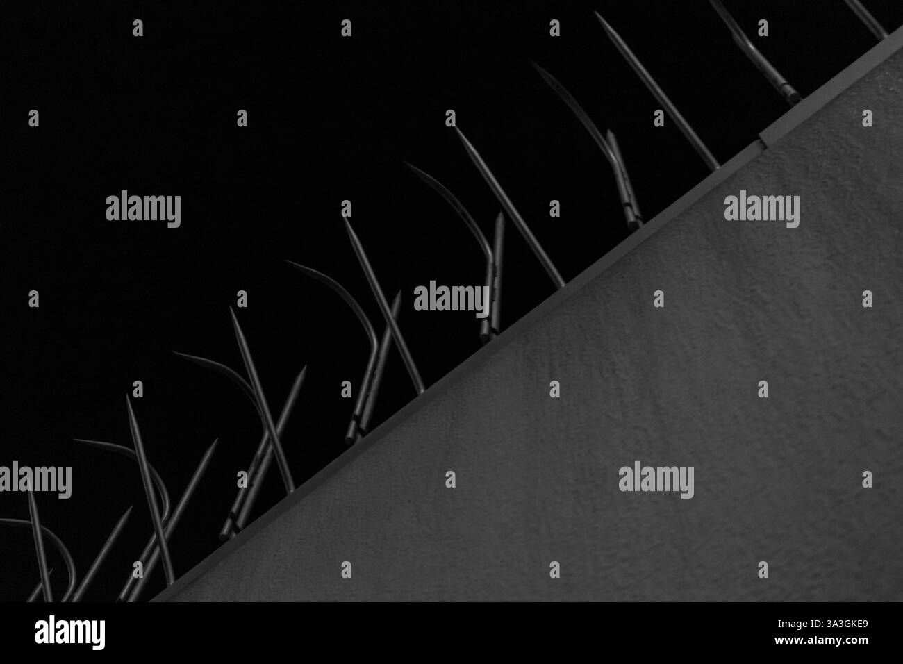 A black-and-white image of a concrete wall with sharp metal security ...