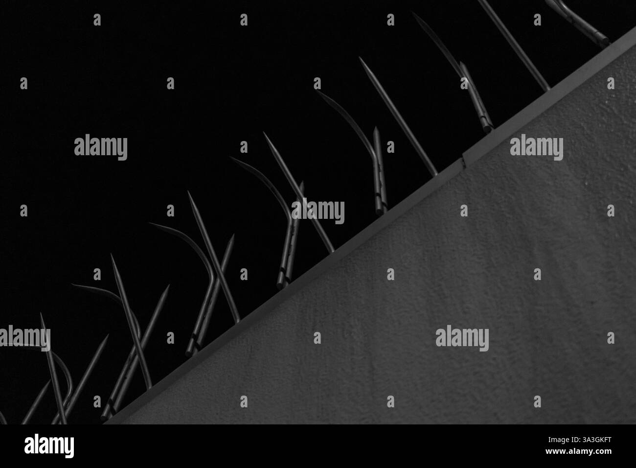 A black-and-white image of a concrete wall with sharp metal security ...
