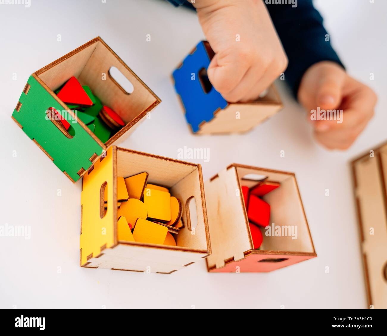 A childs hands sort flat geometric shapes by color into four boxes: red ...