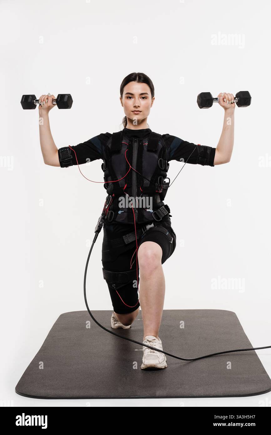Fit girl with dumbbells in EMS suit that uses electrical impulses to ...