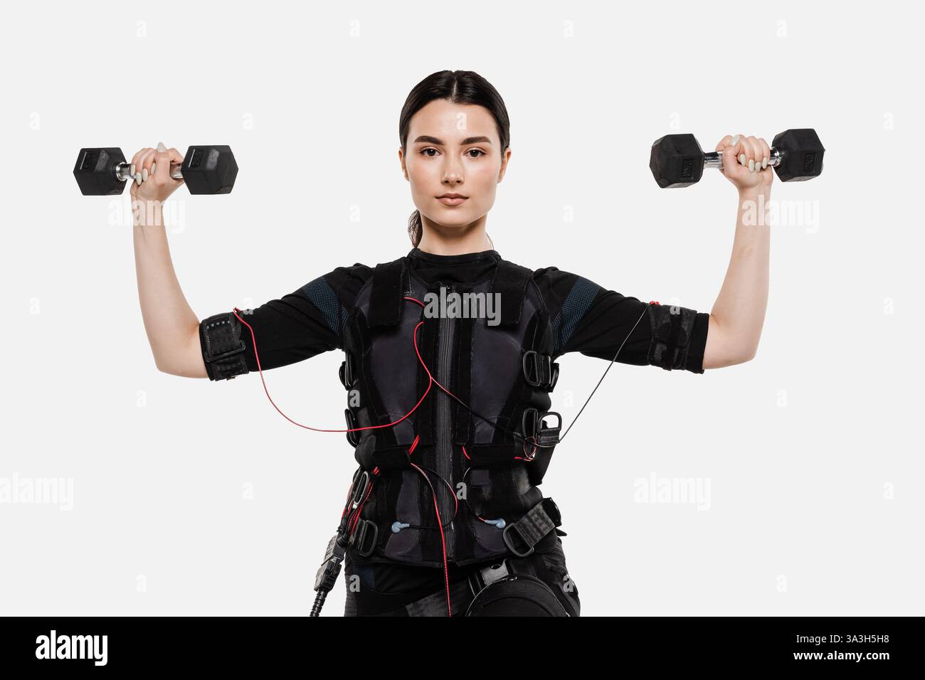 Fit girl with dumbbells in EMS suit that uses electrical impulses to ...