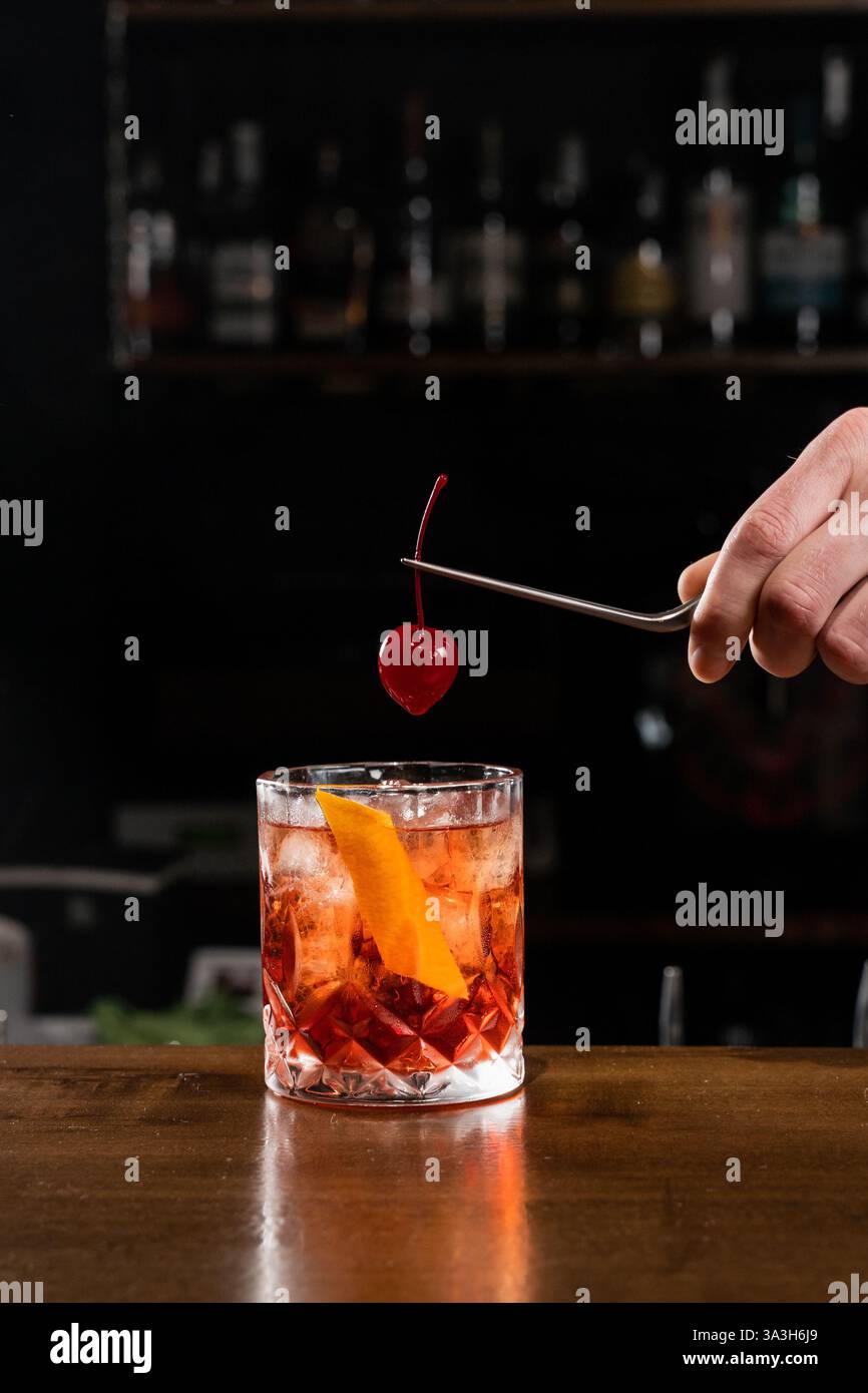 Bartender is holding cherry over Negroni cocktail in the glass. Barman ...