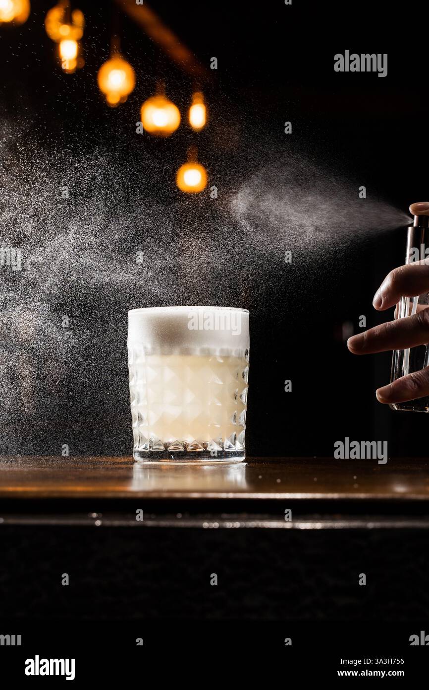 Penicillin classic cocktail in the glass. Bartender is spraying whiskey ...