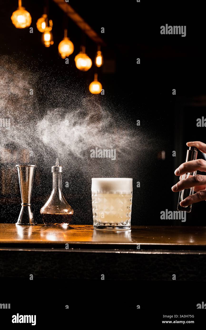 Penicillin classic cocktail in the glass. Bartender is spraying whiskey ...