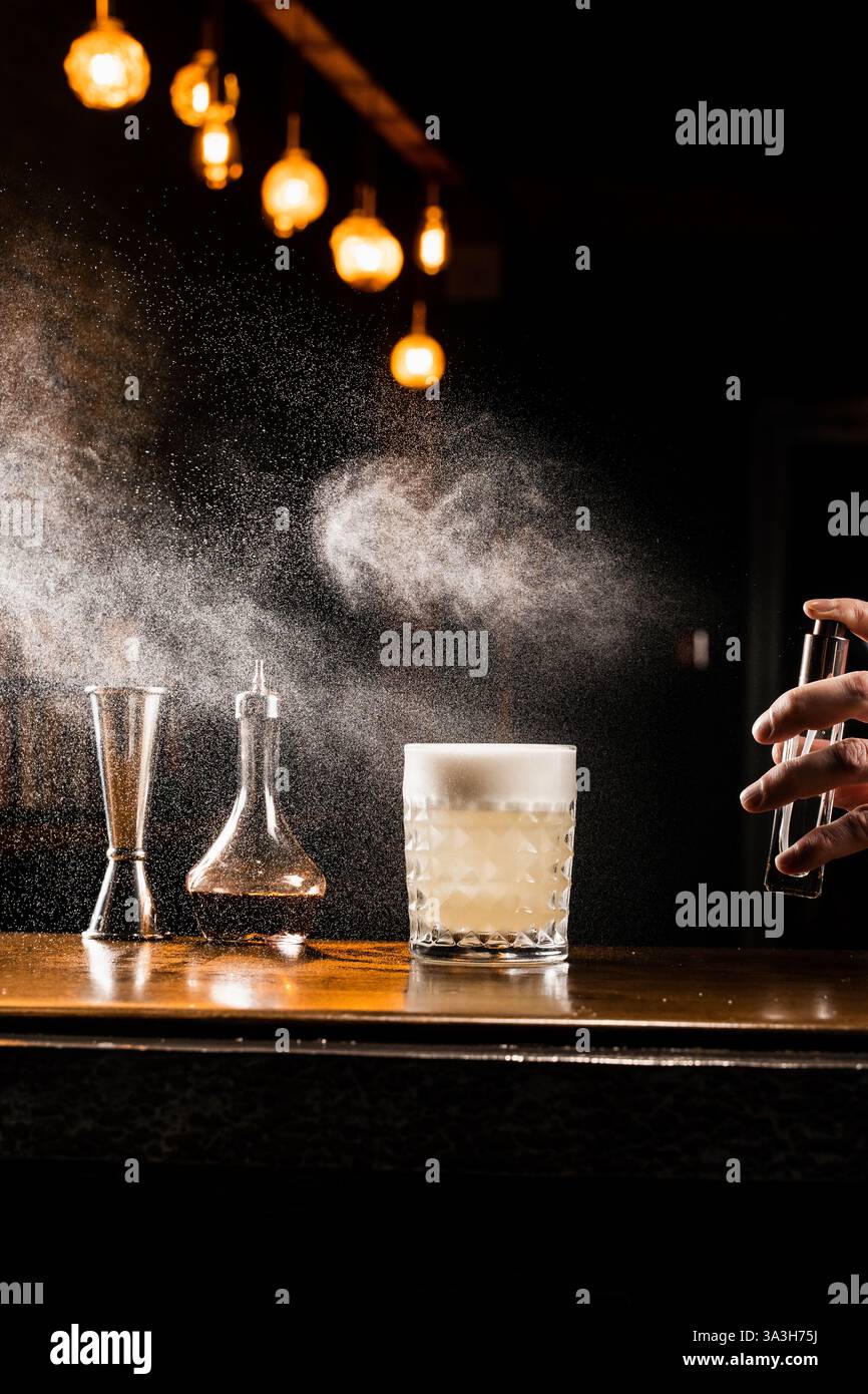 Bartender is spraying whiskey over Penicillin cocktail in the bar ...