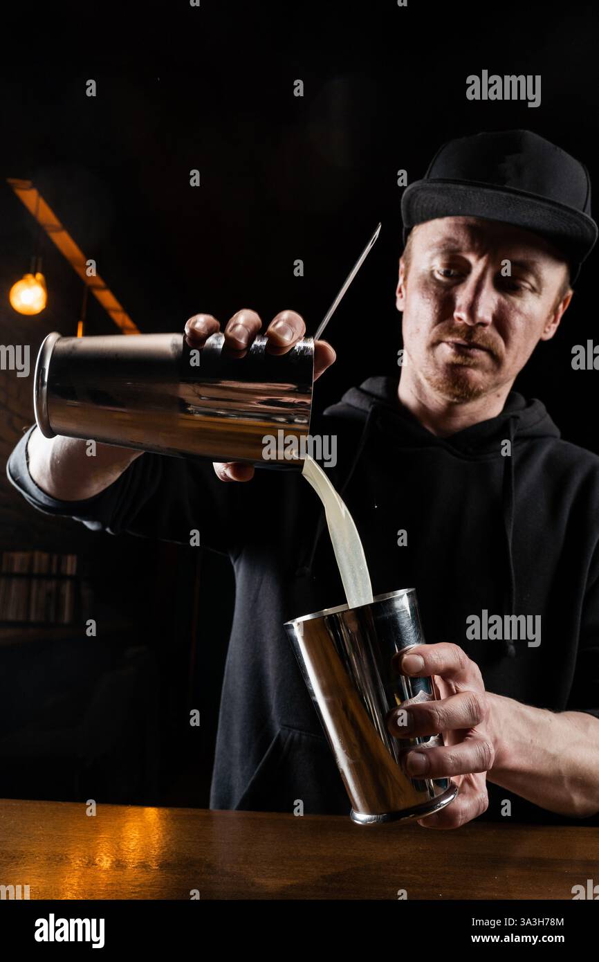 Bartender is pouring and mixing Penicillin cocktail at the bar. Bartender mixes whiskey, lemon ...