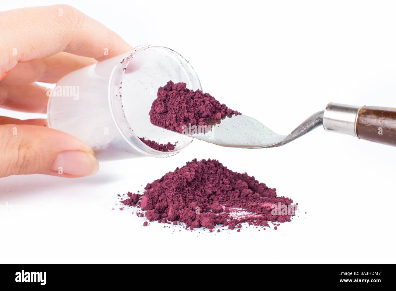 A hand holds a small container while a knife scoops vibrant purple ...
