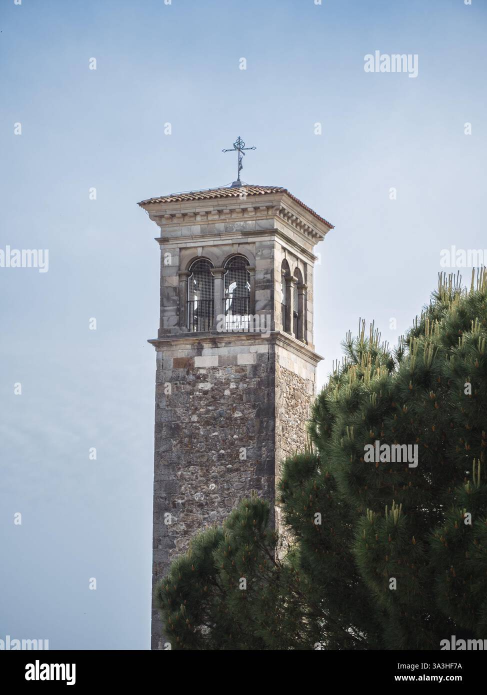 A historic stone bell tower with arched windows and a metal cross on ...