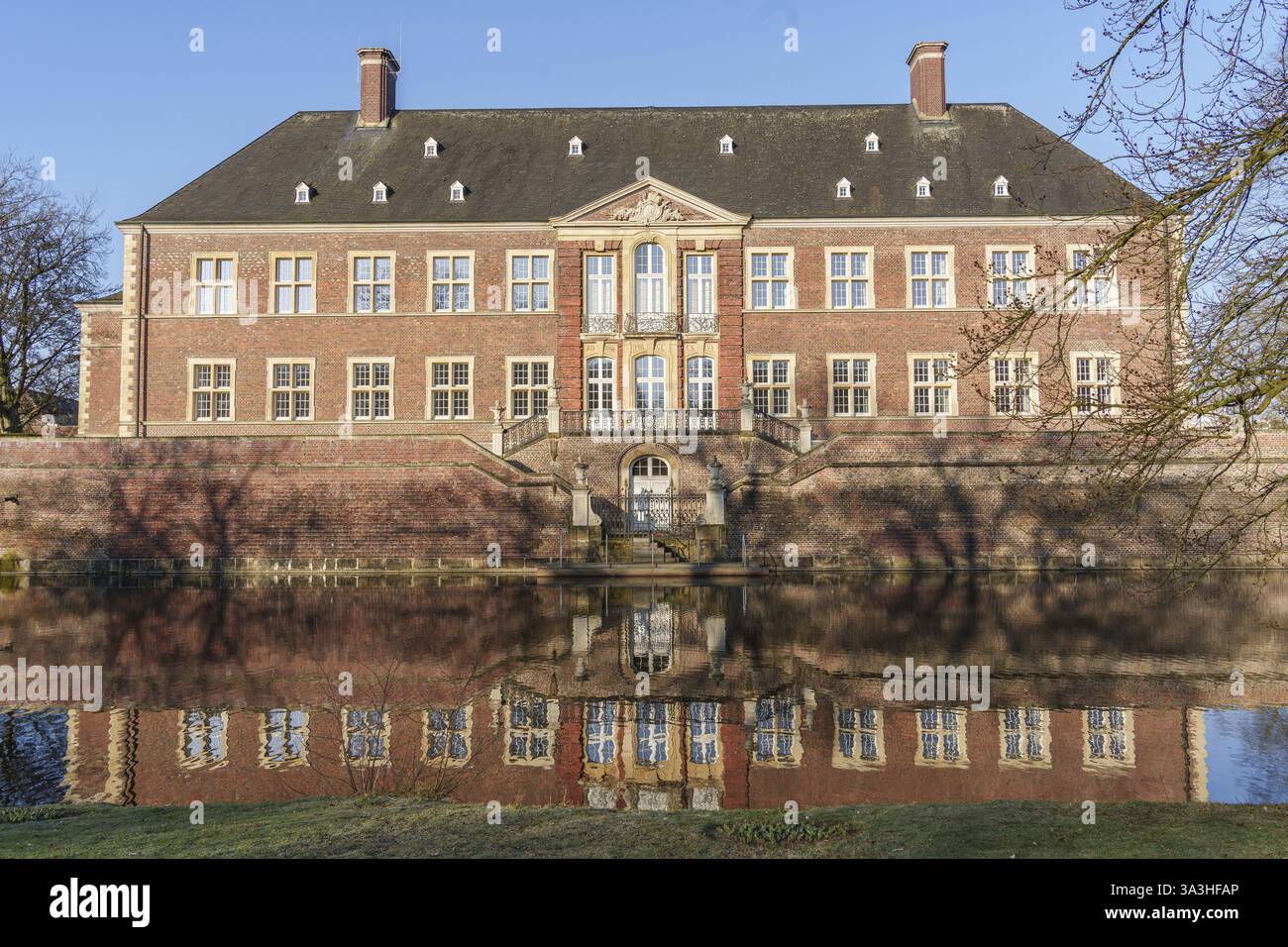 Large baroque castle with symmetrical brick facade reflected in a moat ...