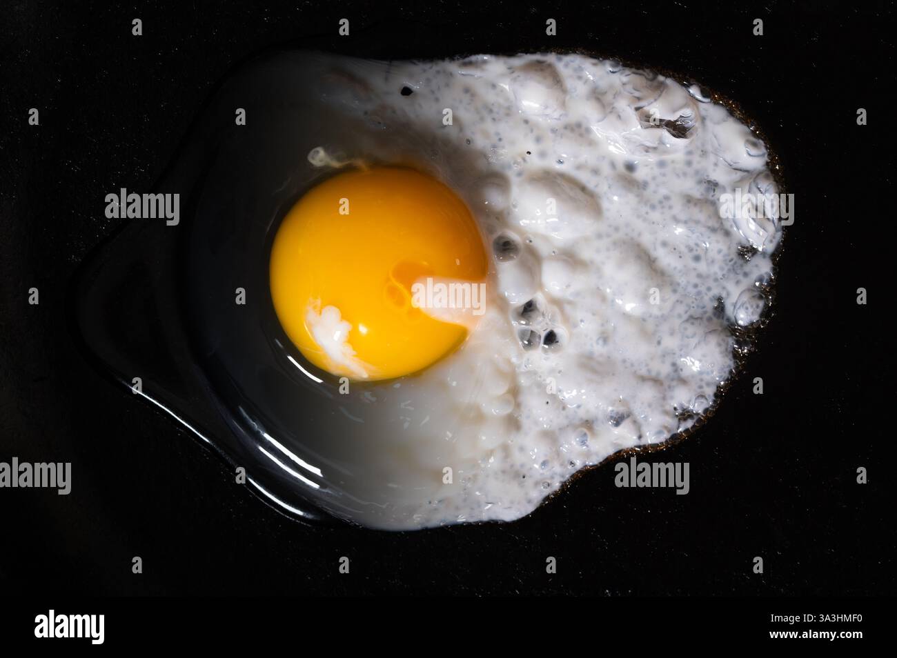 An egg in a cast iron pan, raw on the left side and cooked on the right ...