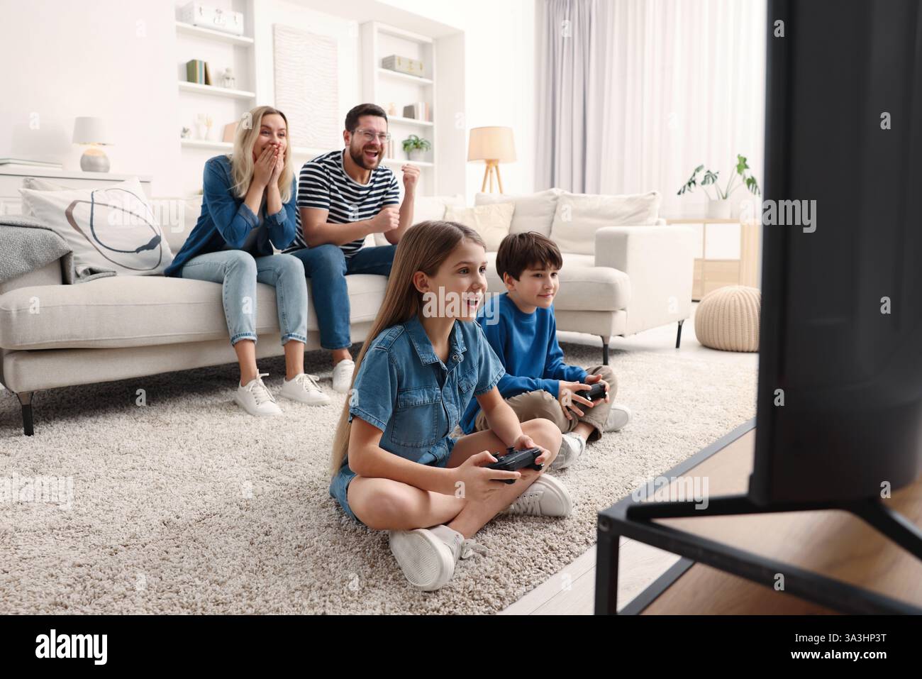 Cute kids playing video games while their parents resting on sofa ...