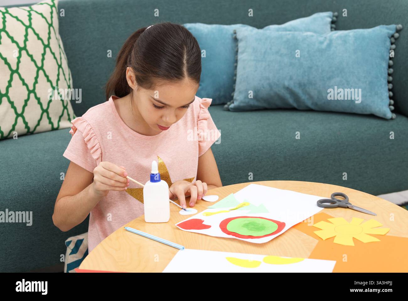 Girl applying glue onto paper figure for her creative project at table ...