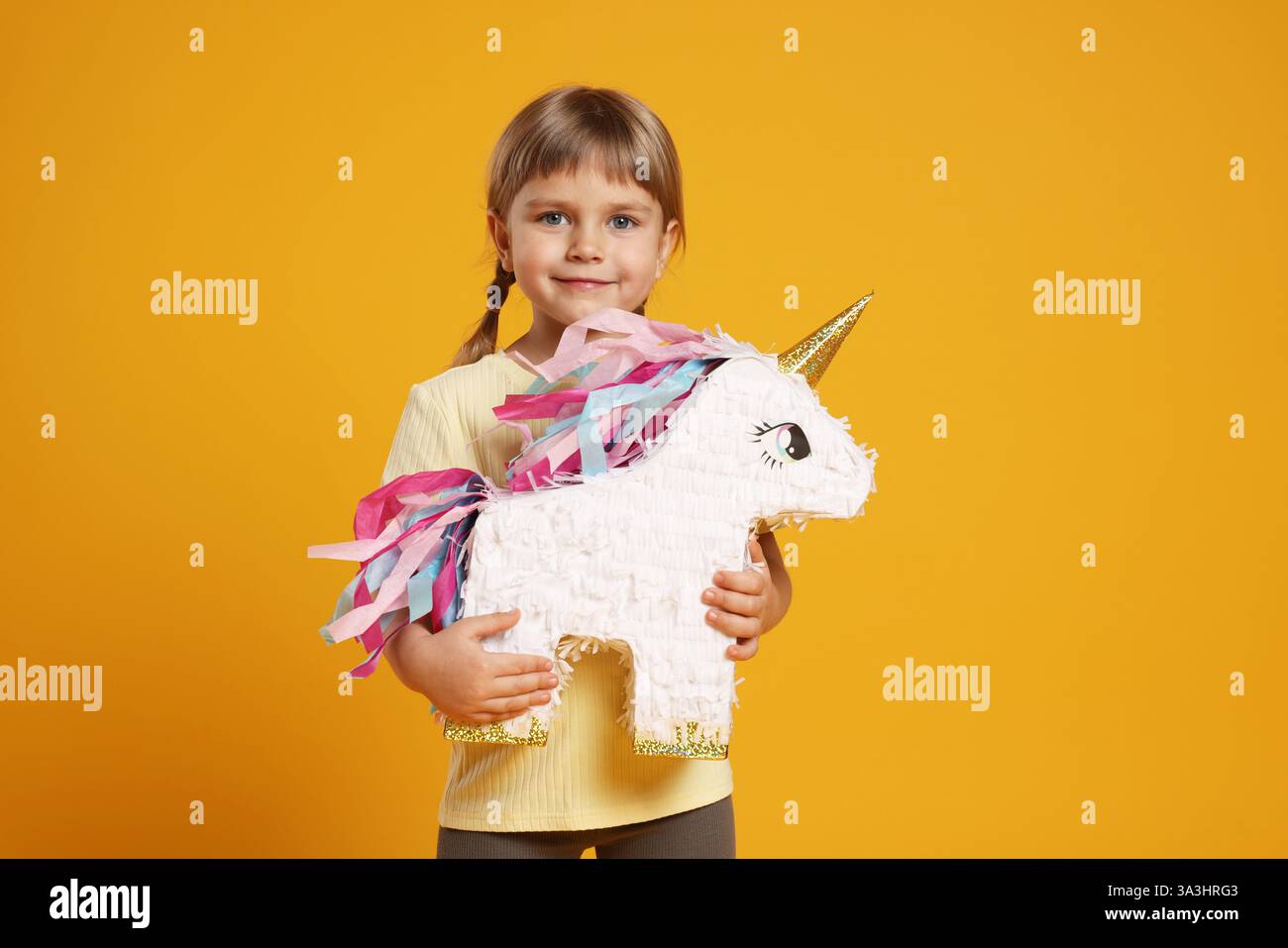 Cute girl with unicorn shaped pinata on orange background Stock Photo ...