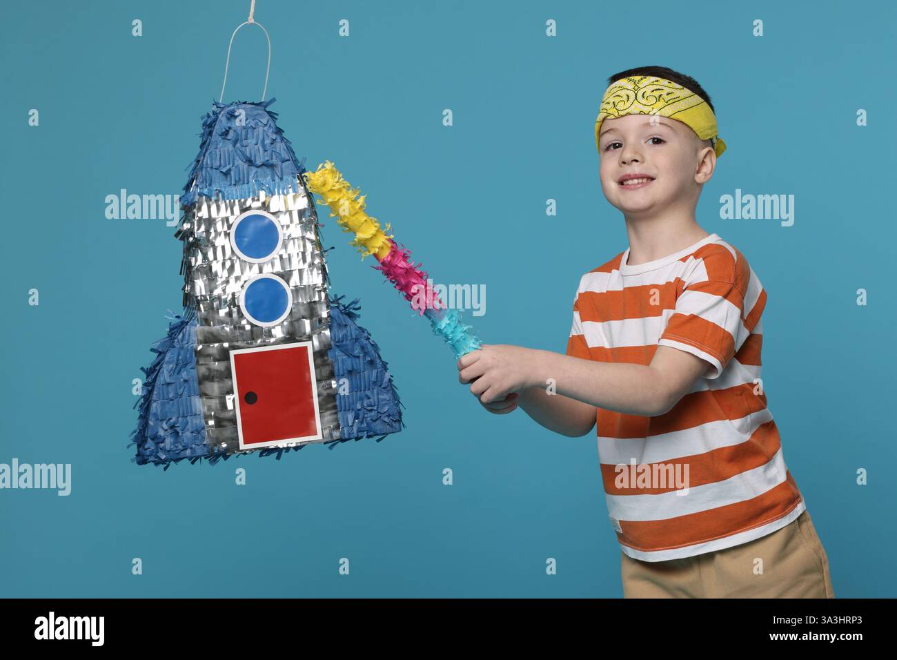 Happy boy breaking rocket shaped pinata with stick on light blue ...