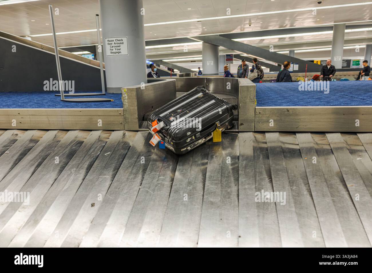 Black suitcase with baggage tags moving from conveyor onto baggage ...
