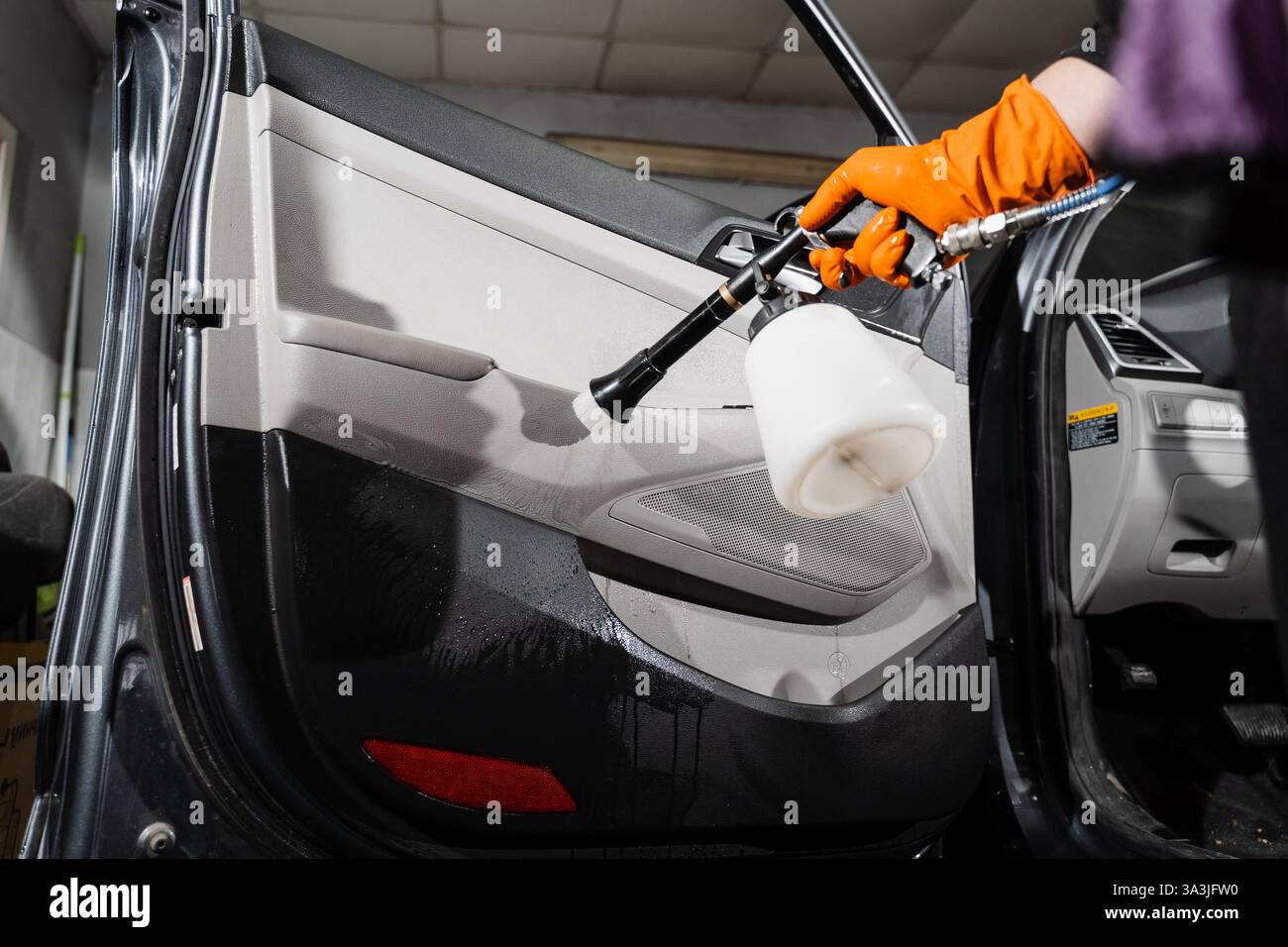 Cleaner is washing car door card panel and spraying detergent from tornador gun. Car detailing ...