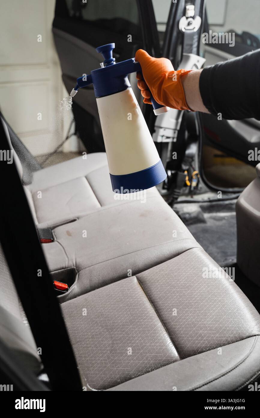 Professional cleaner in gloves is pouring detergent on seat in car for ...
