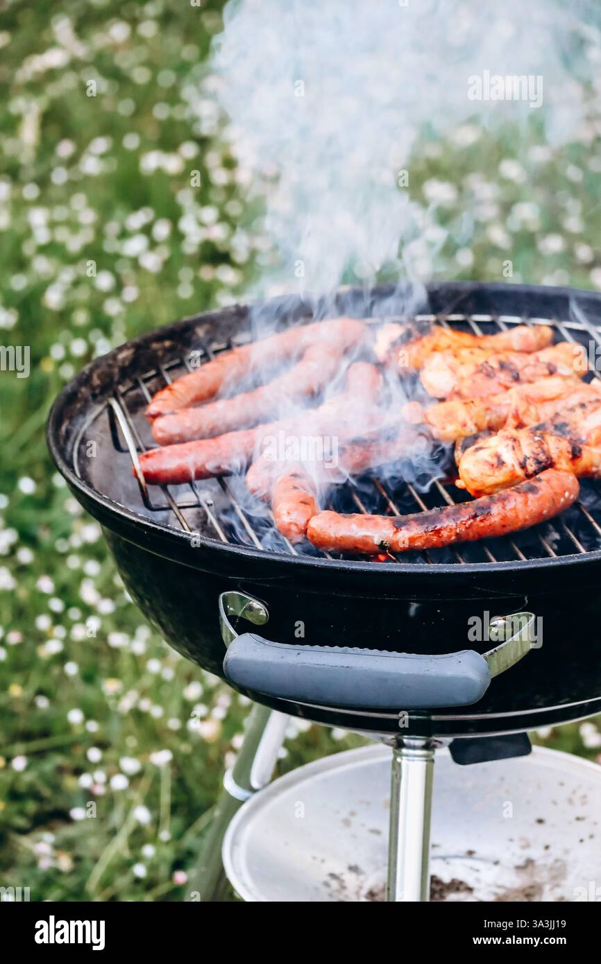 Chicken legs and merguez sausages cooking on a barbecue in the garden ...
