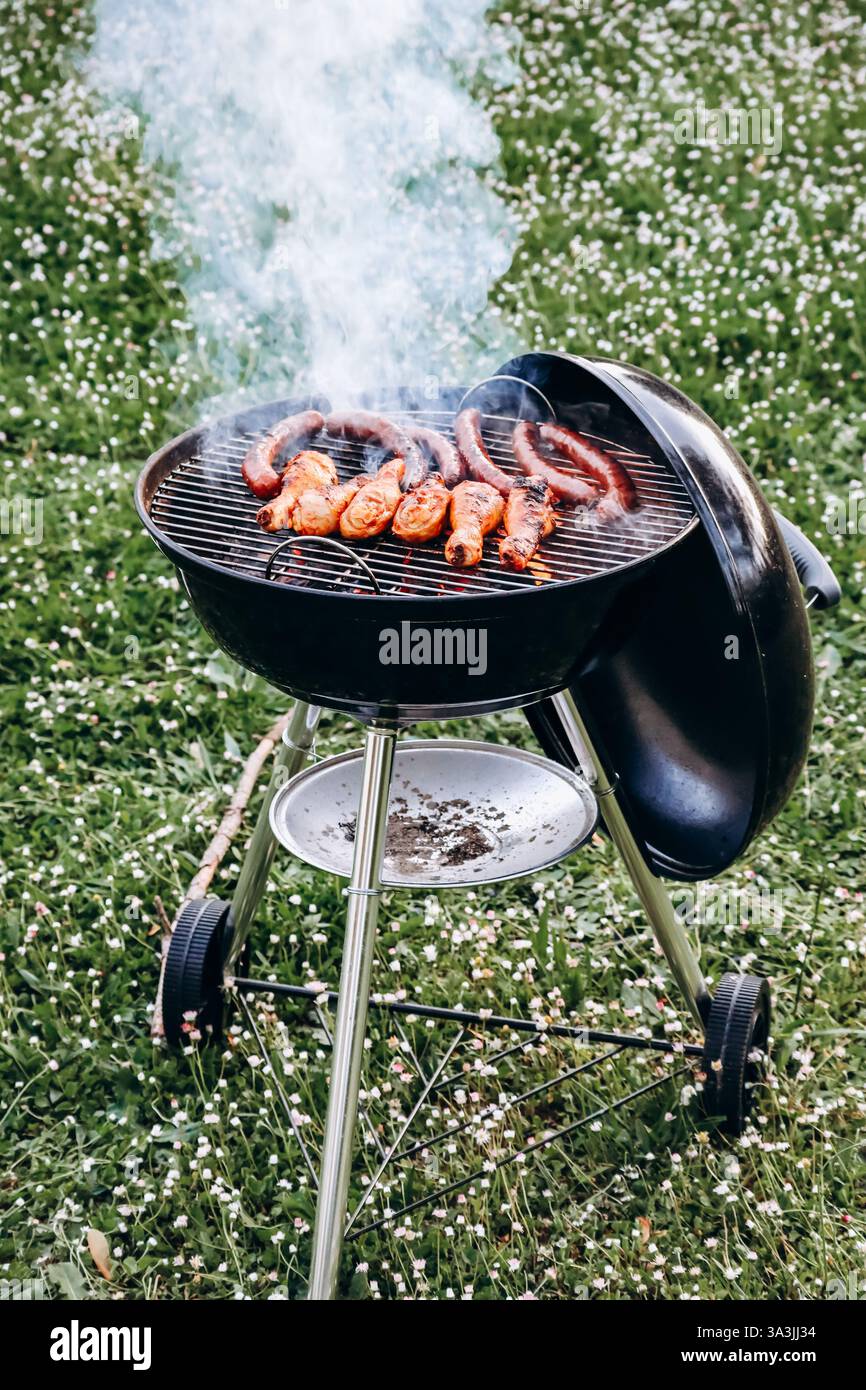 Chicken legs and merguez sausages cooking on a barbecue in the garden ...