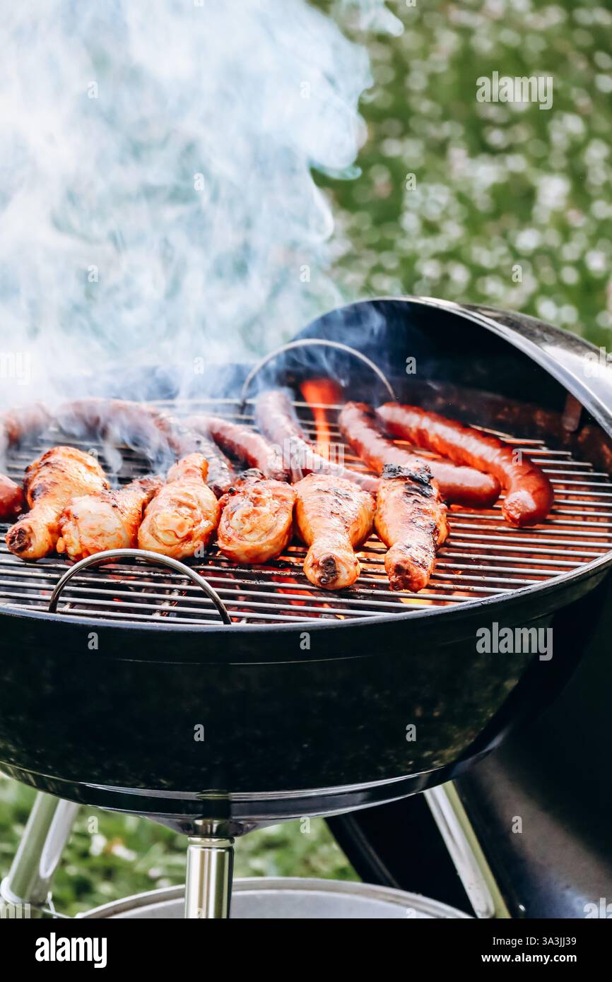 Chicken legs and merguez sausages cooking on a barbecue in the garden ...