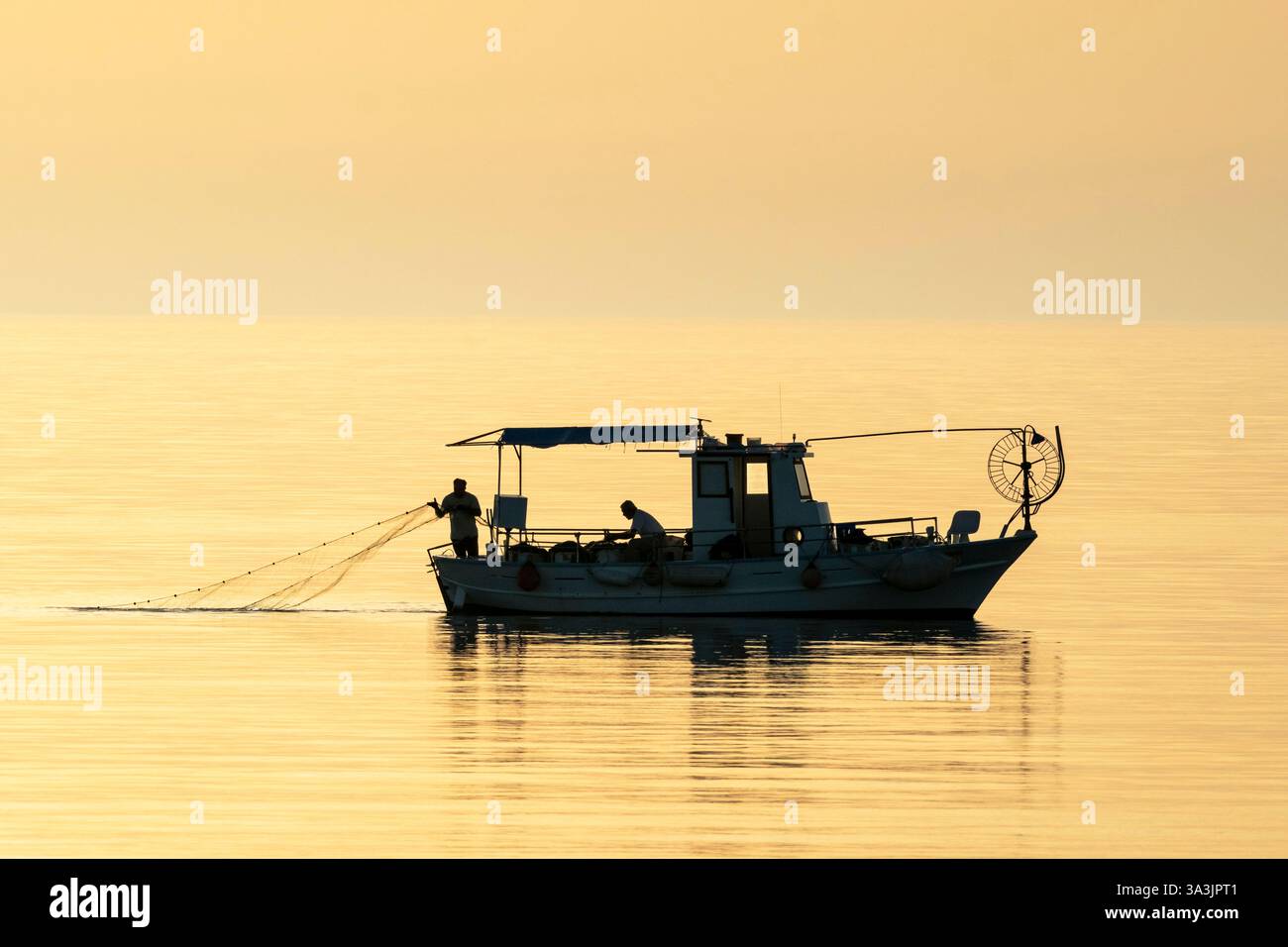 Traditional Cypriot caique fishing boat setting its nets at sunset ...