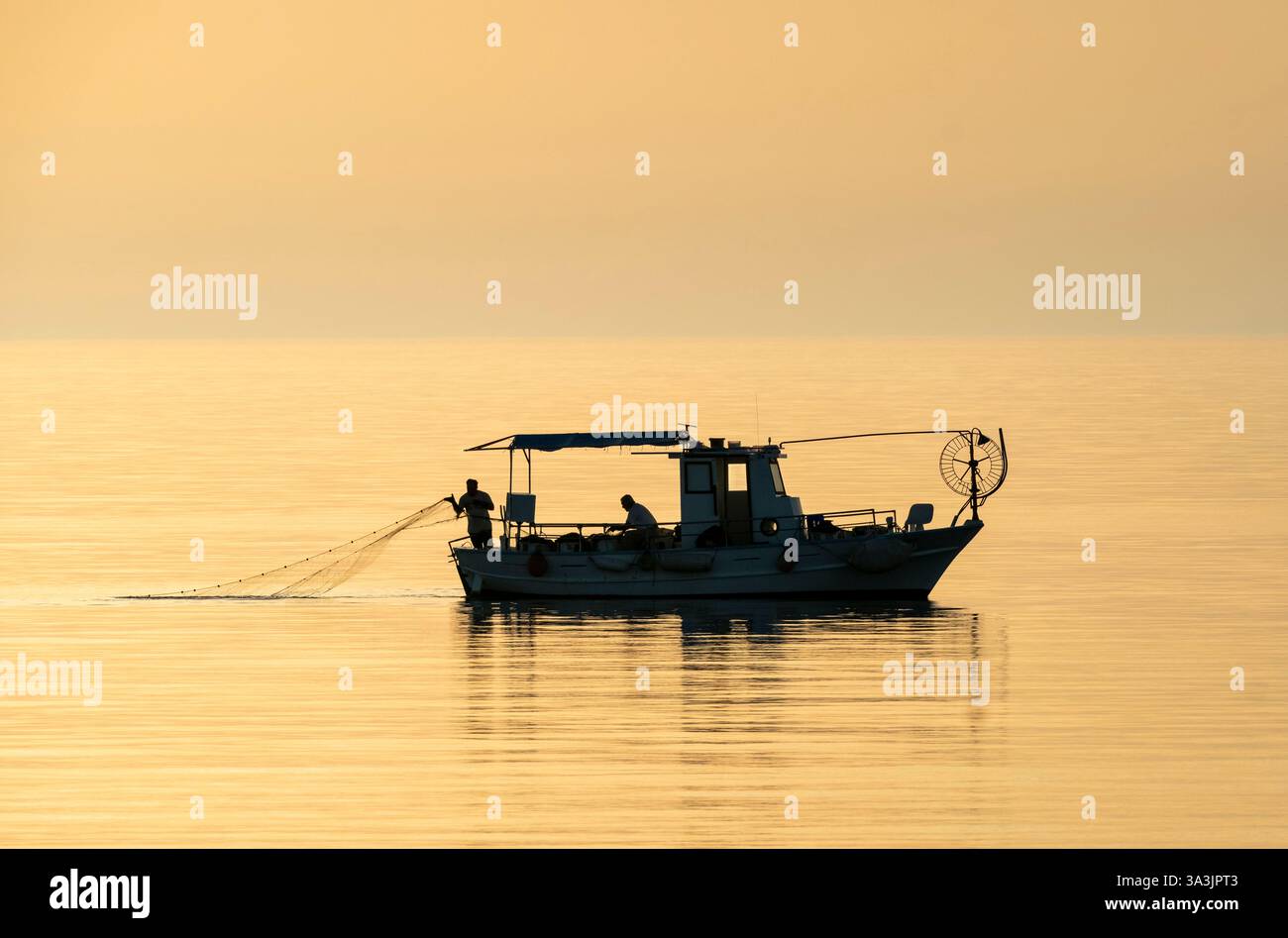 Traditional Cypriot caique fishing boat setting its nets at sunset ...