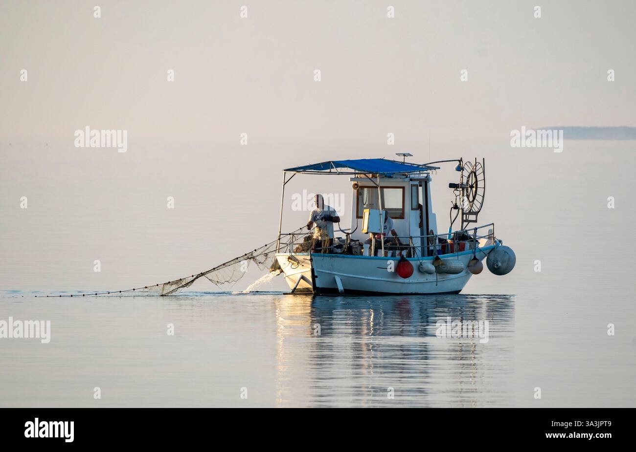 Traditional Cypriot caique fishing boat setting its nets at sunset ...