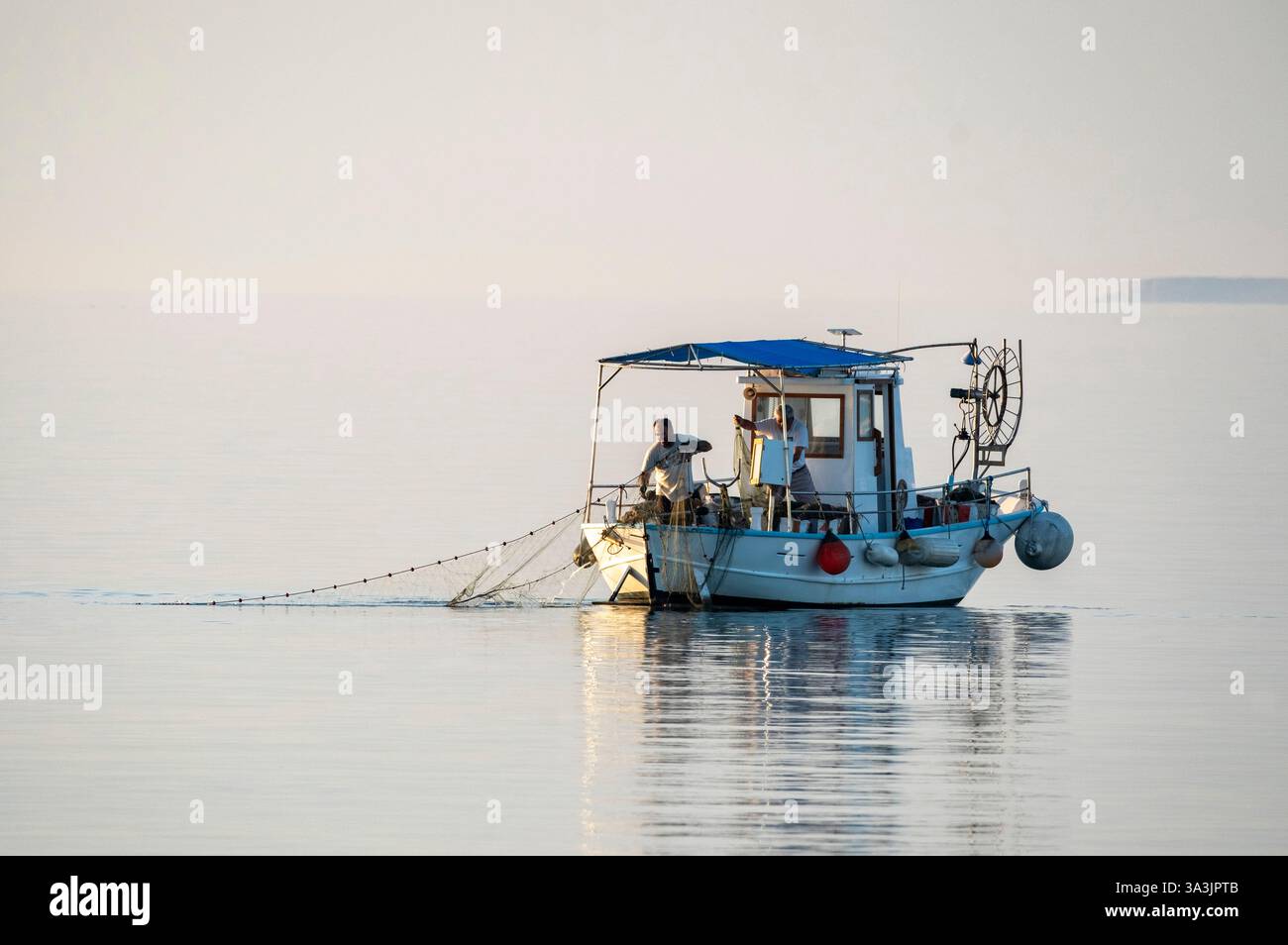 Traditional Cypriot caique fishing boat setting its nets at sunset ...