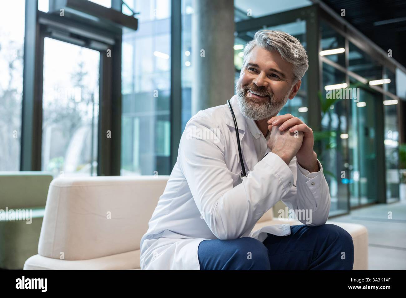 Smiling doctor in lab coat sitting on the sofa in a clinic hall Stock ...