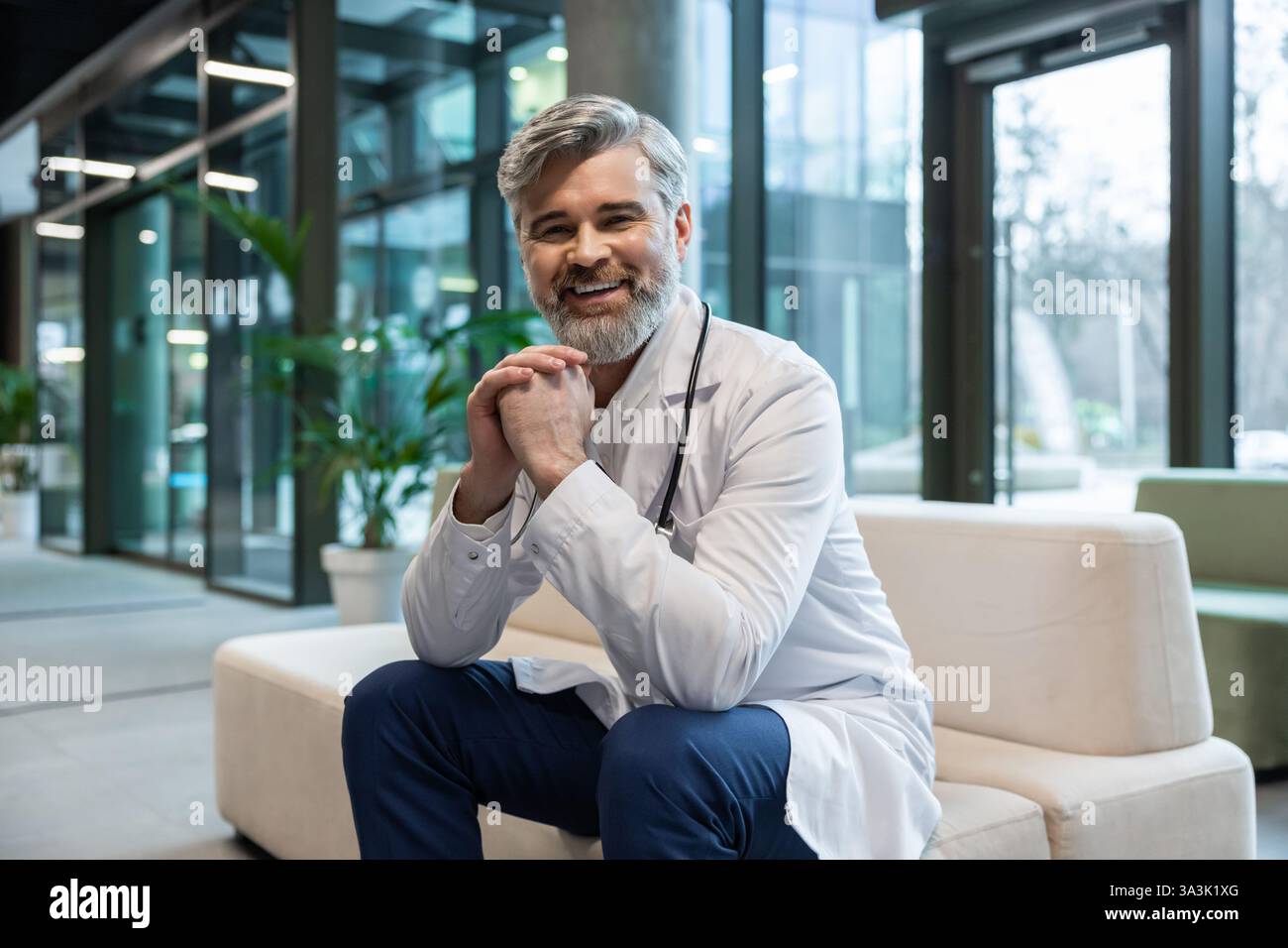 Smiling doctor in lab coat sitting on the sofa in a clinic hall Stock ...