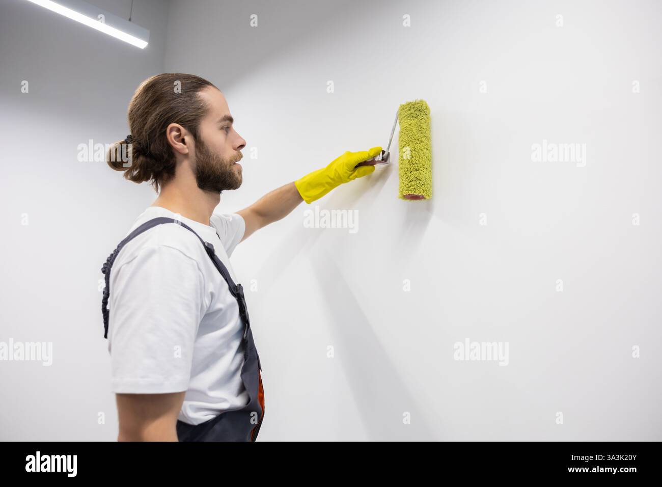 Dark-haired young bearded man in yellow gloves painting the wall Stock ...
