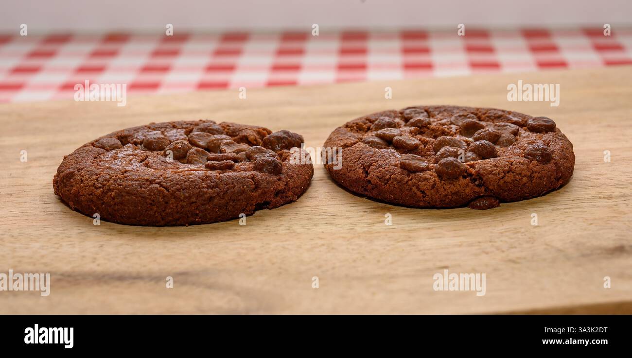 Two warm chocolate chip cookies sit side by side on a wooden surface ...