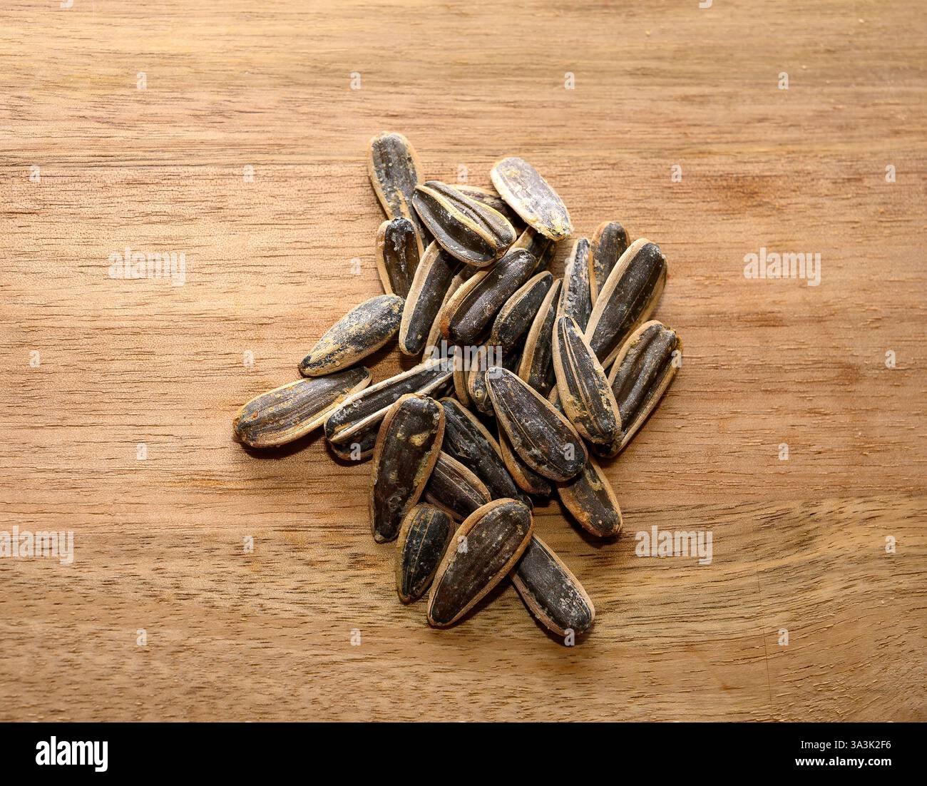 A collection of sunflower seeds is scattered on a wooden surface. The ...