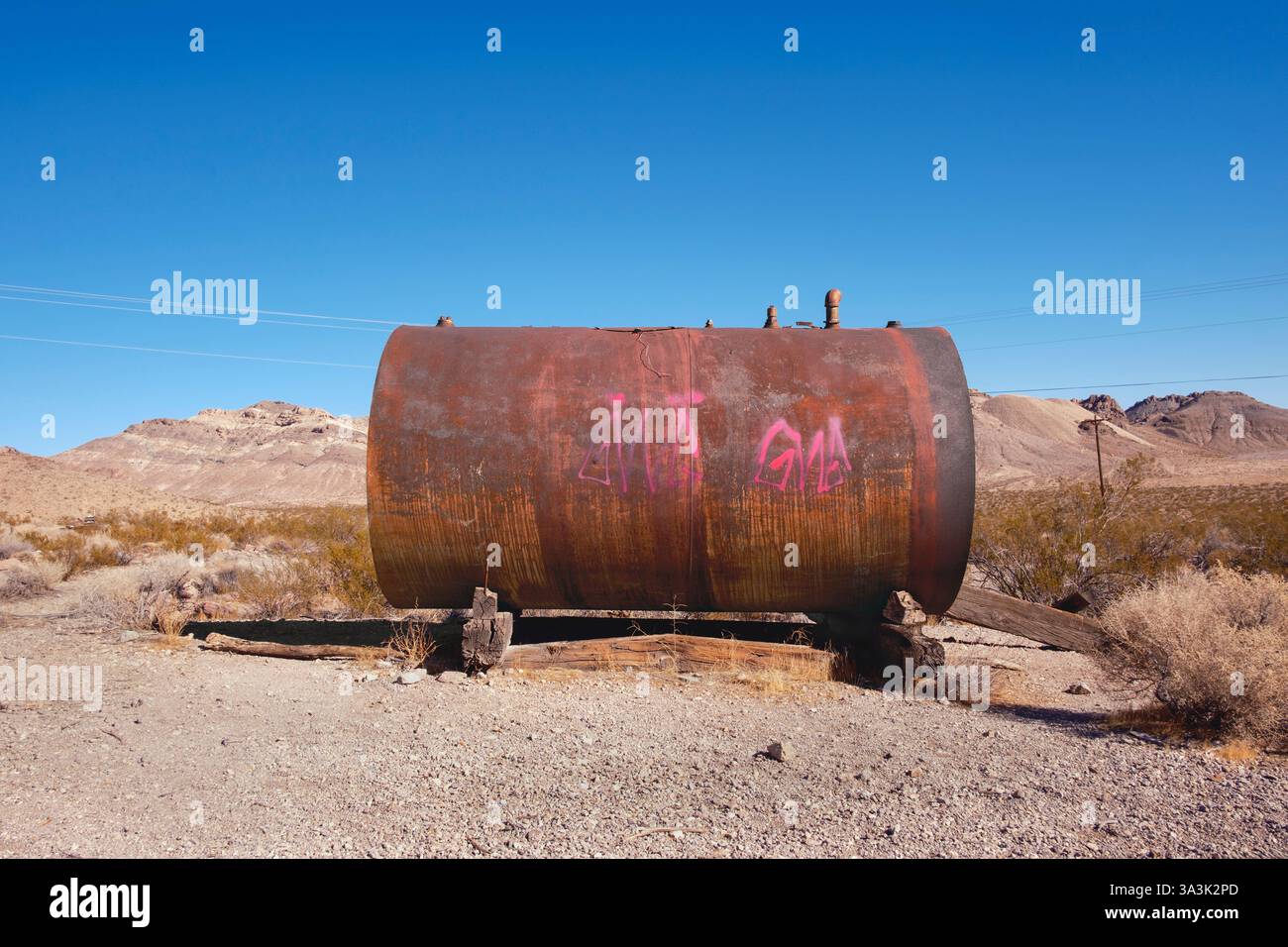 Rusted metal storage tank with painted graffiti in abandoned ghost town ...