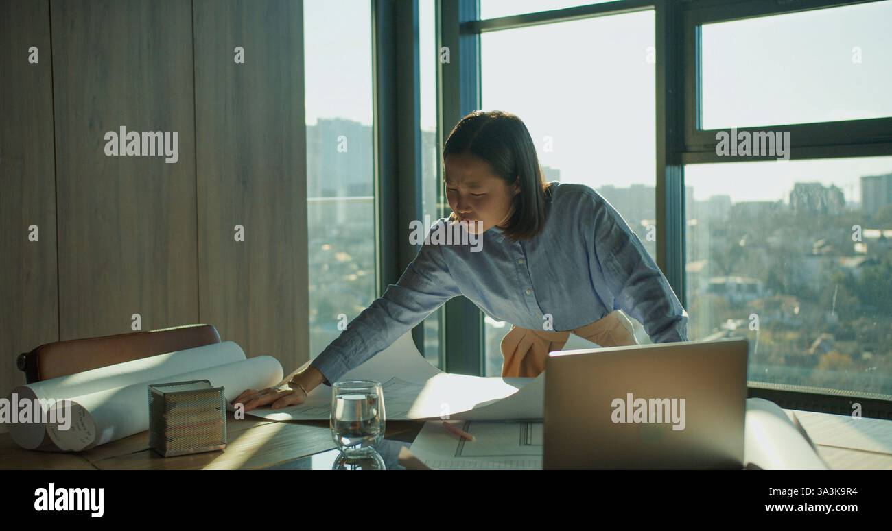 A focused architect analyzing a building floor plan in a well-lit ...