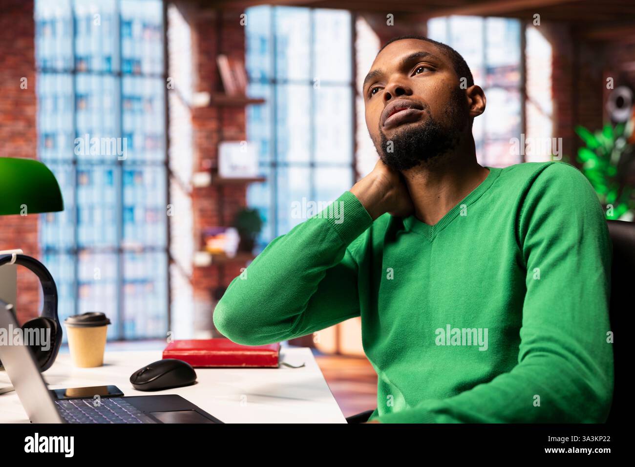 Remote worker in home office stretching neck after sitting at desk too ...
