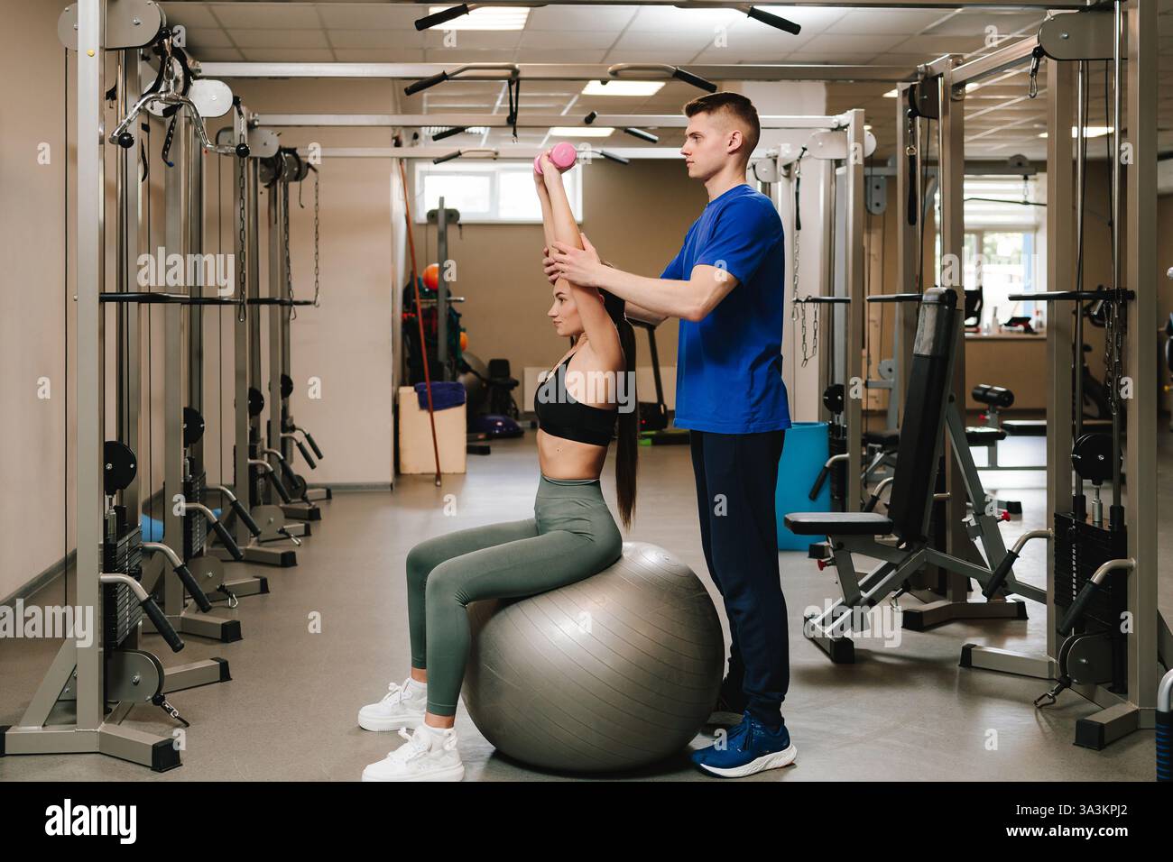 Kinesiotherapy. Young woman is doing supervised therapeutic gymnastics on exercise ball. Doing ...