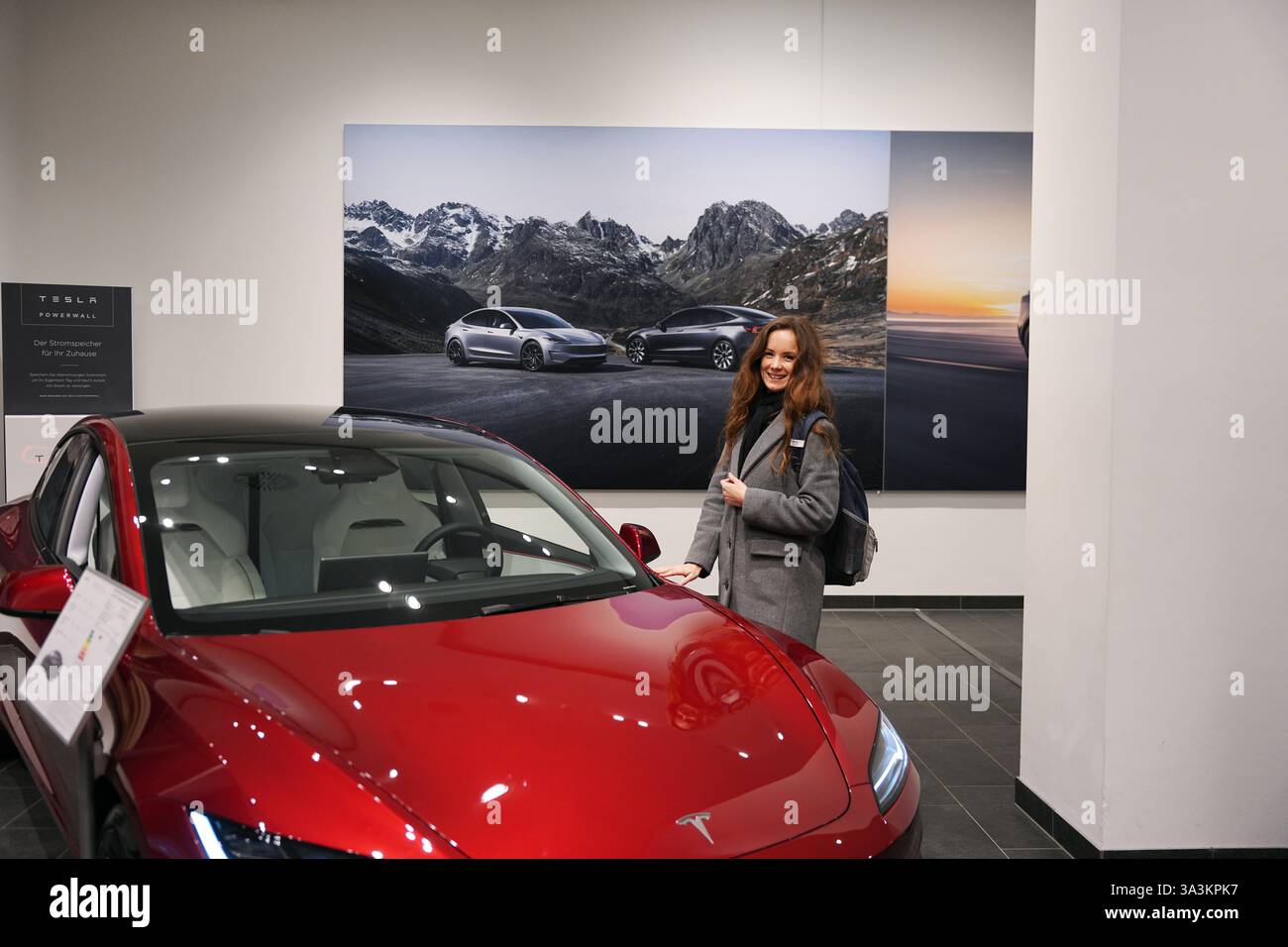Berlin, Germany 02.13.2025 Smiling woman admiring red Tesla Model 3 ...