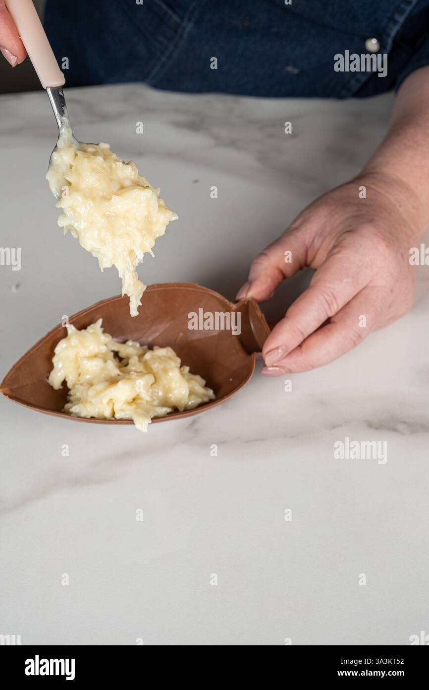 Confectioner putting coconut candy filling in a milk chocolate Easter ...