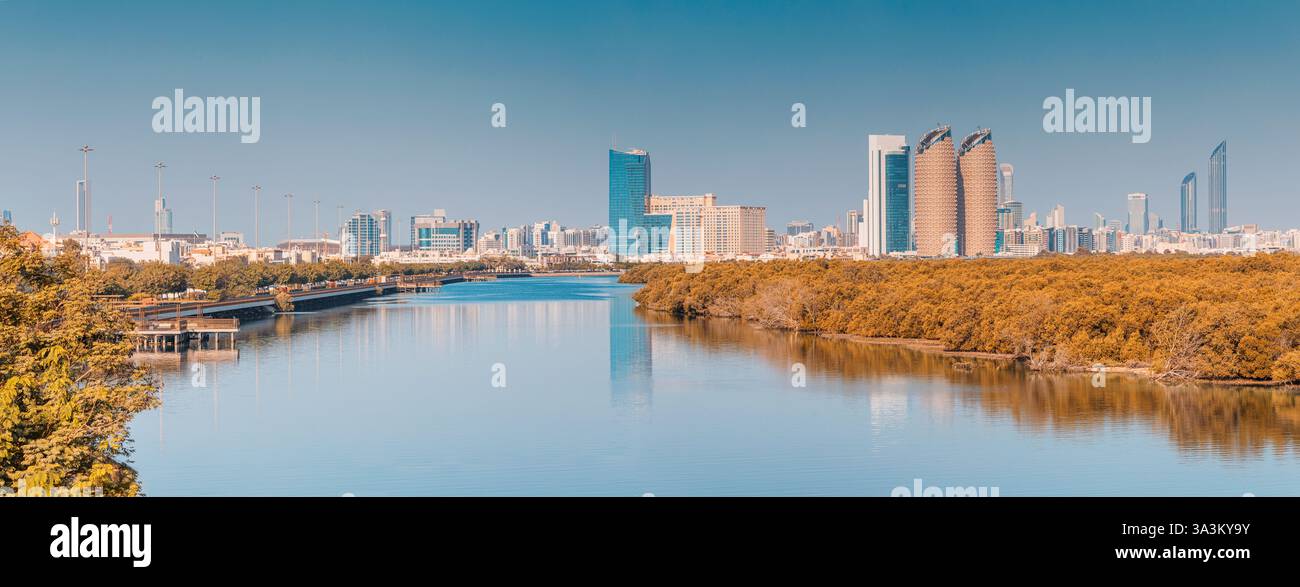 Calm water reflecting Abu Dhabi skyline with modern buildings and lush ...