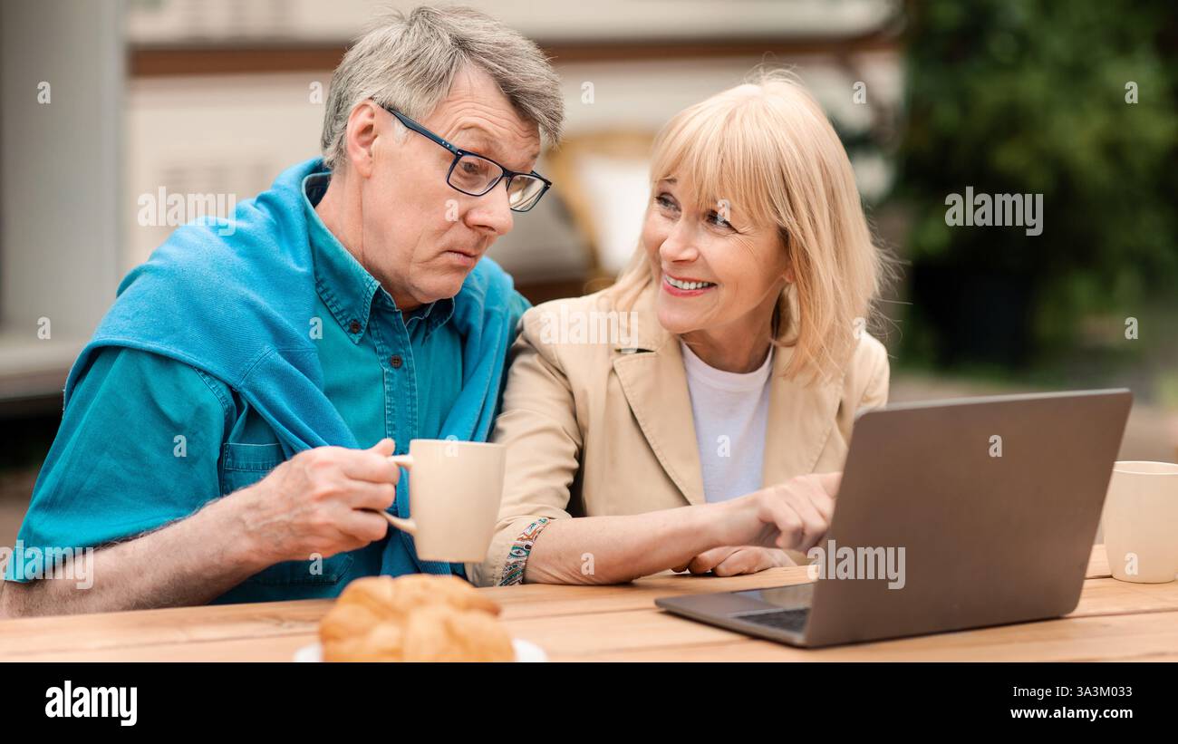Happy senior woman showing something to her husband on laptop computer ...