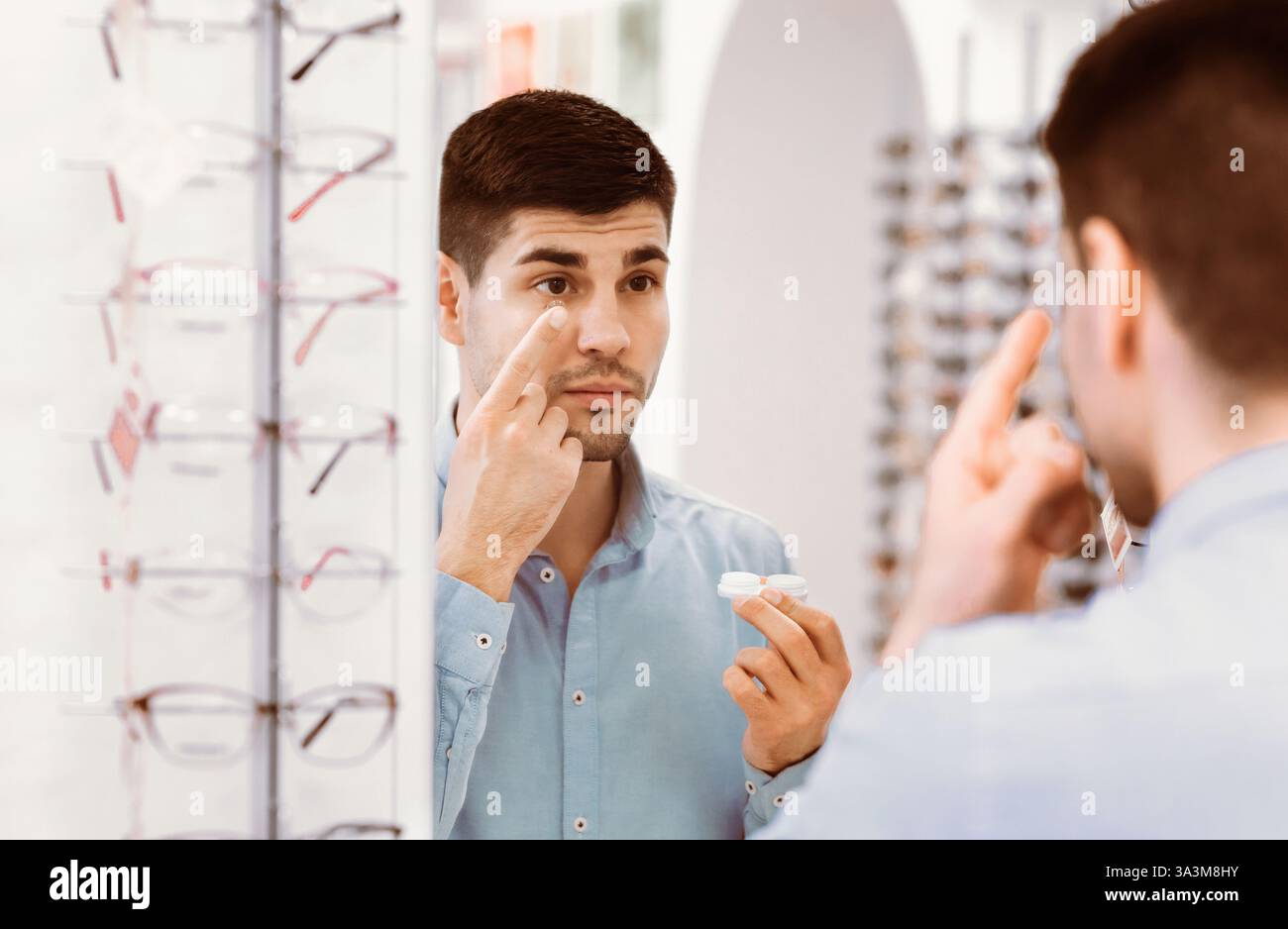 Man applying contact lens solution while trying on glasses in an ...