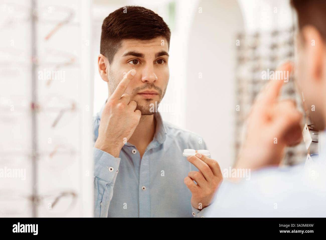 Man applying contact lenses in a store while looking in the mirror ...
