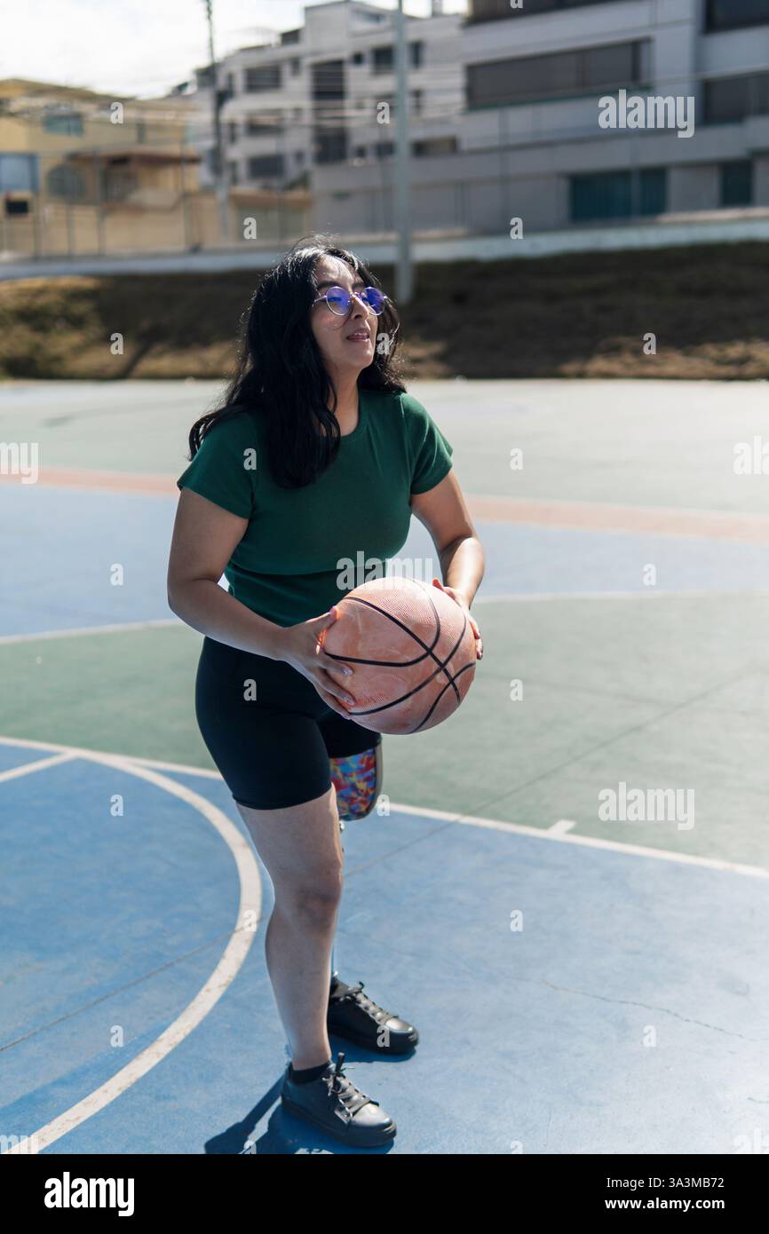 Athletic woman with prosthetic leg is playing basketball on an outdoor ...