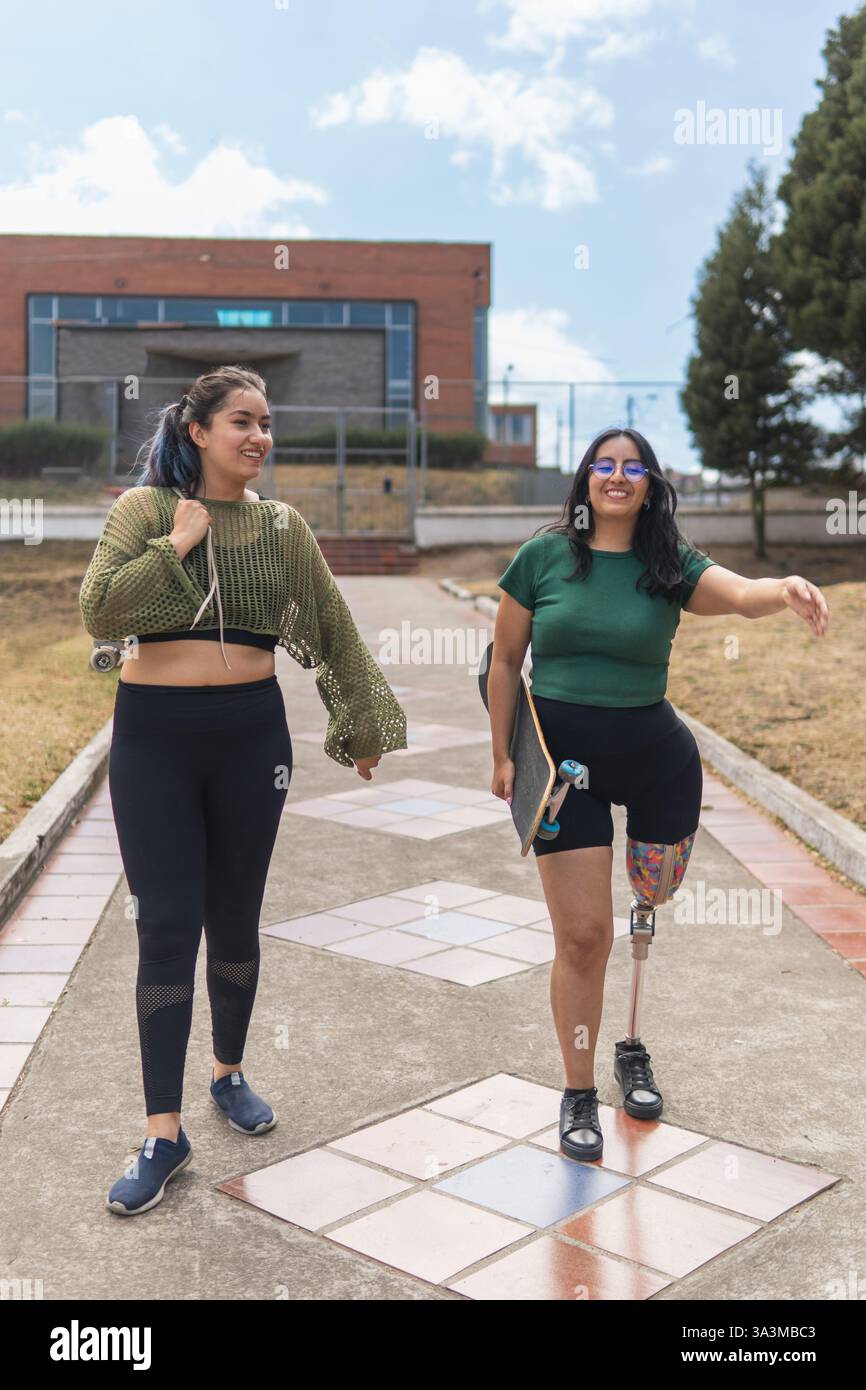 Two happy female friends with skateboards walking in the park, one of ...